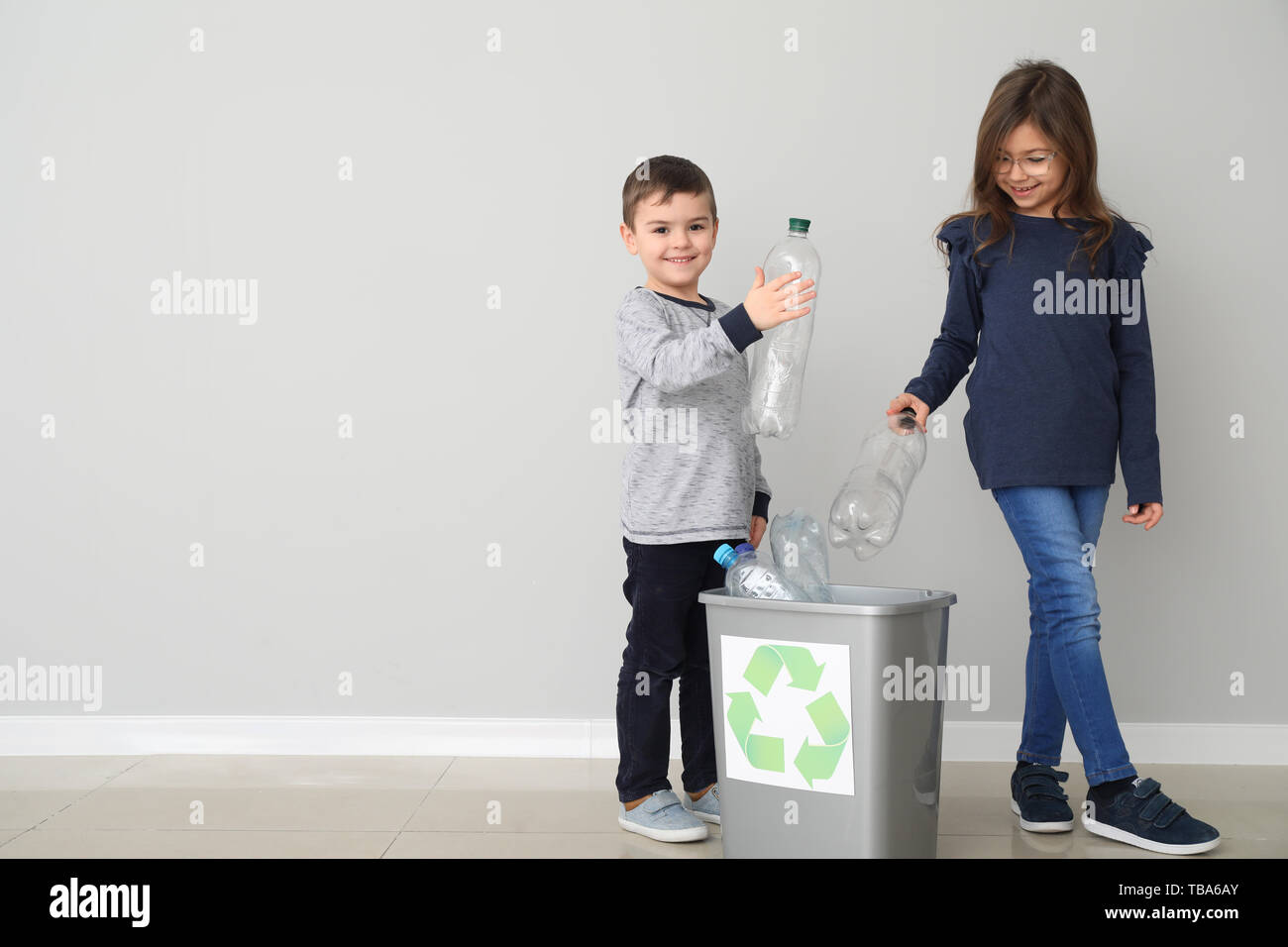 Children throwing garbage into trash bin near light wall. Recycling ...