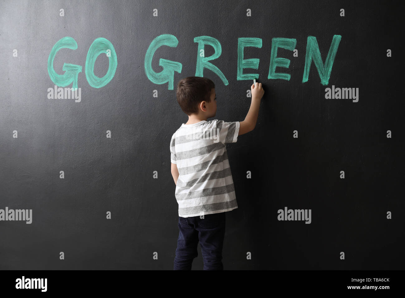 Little boy writing text GO GREEN on dark wall Stock Photo - Alamy