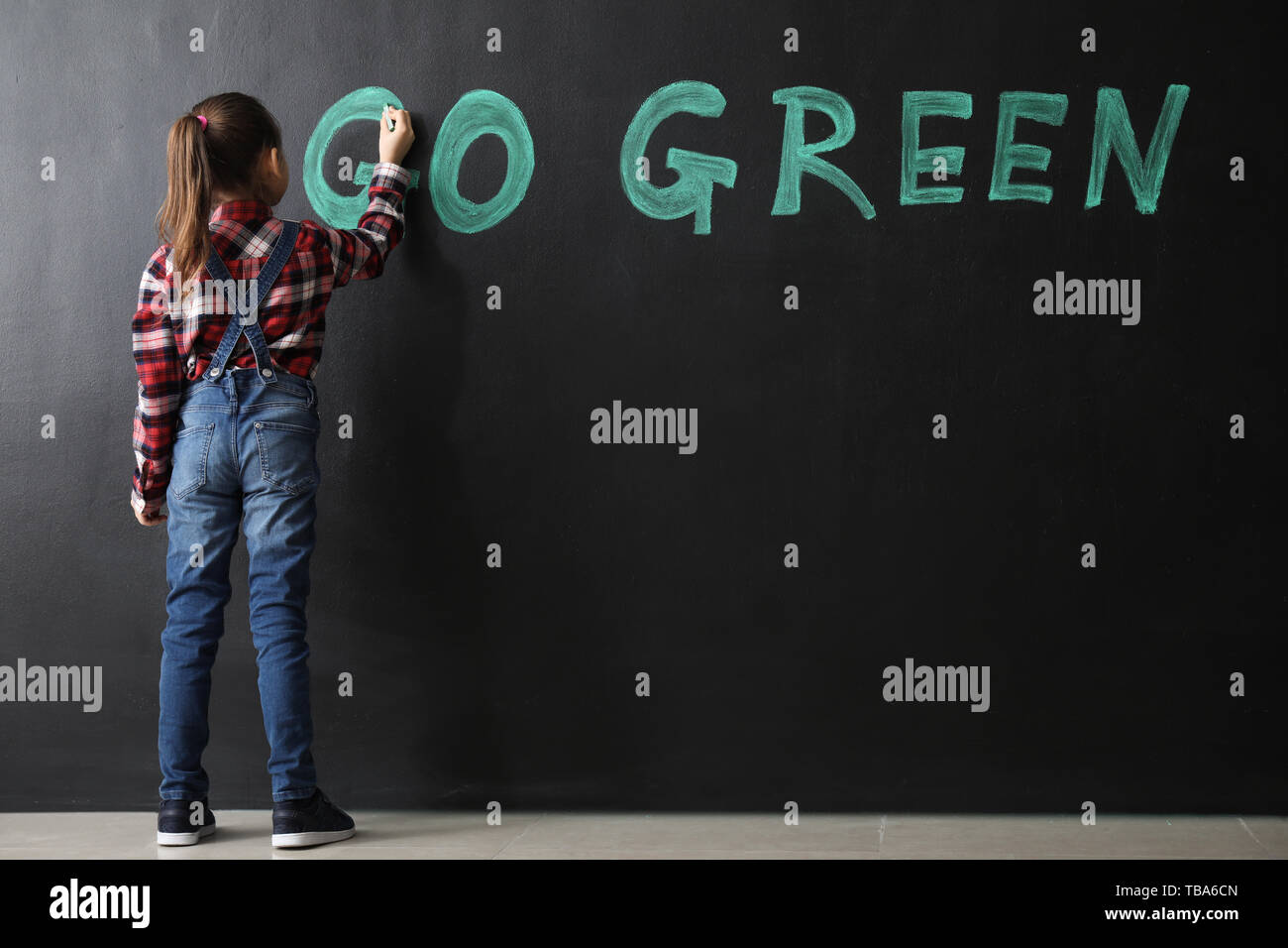 Little girl writing text GO GREEN on dark wall Stock Photo - Alamy