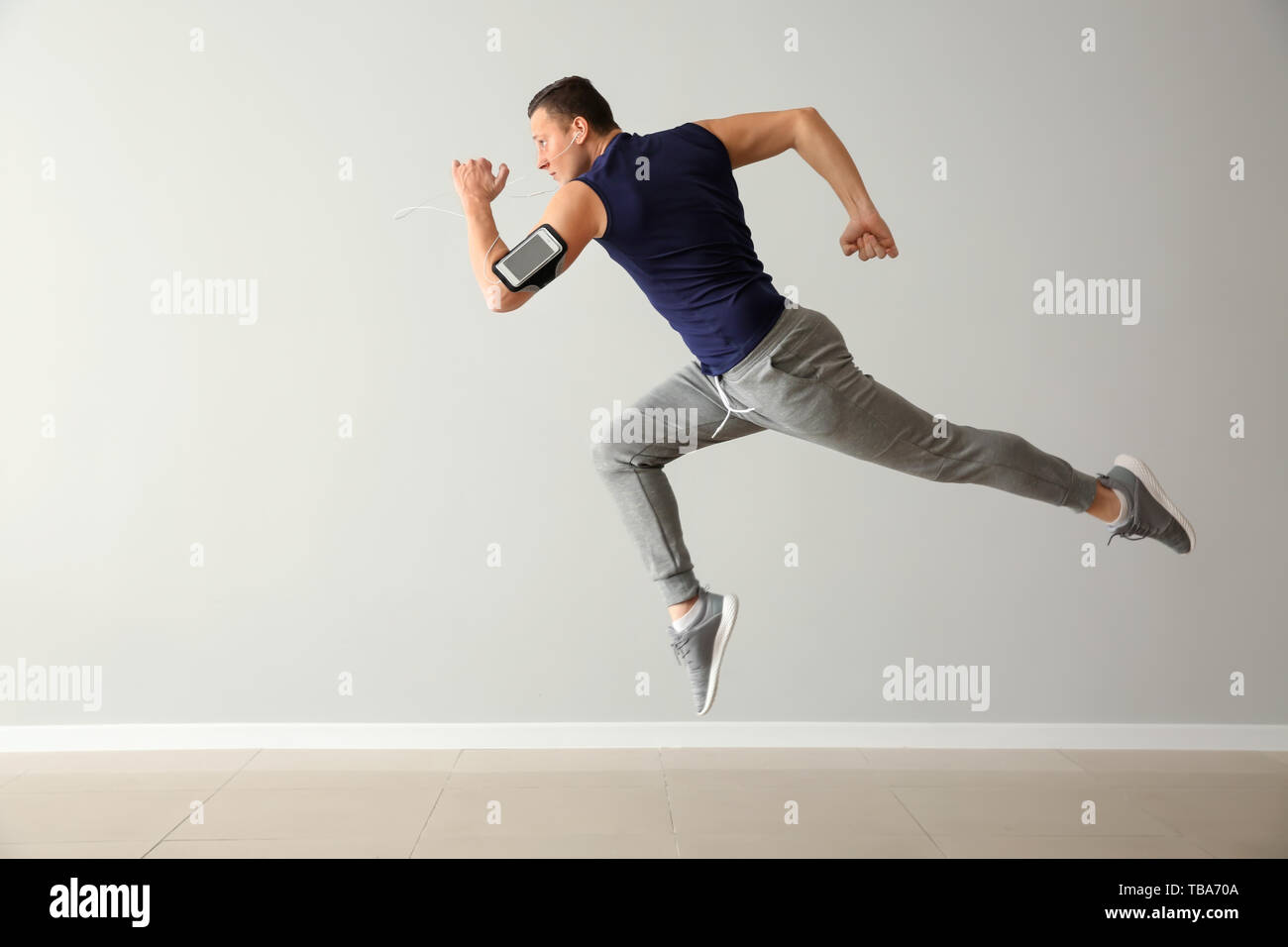 Sporty young man running against light wall Stock Photo - Alamy