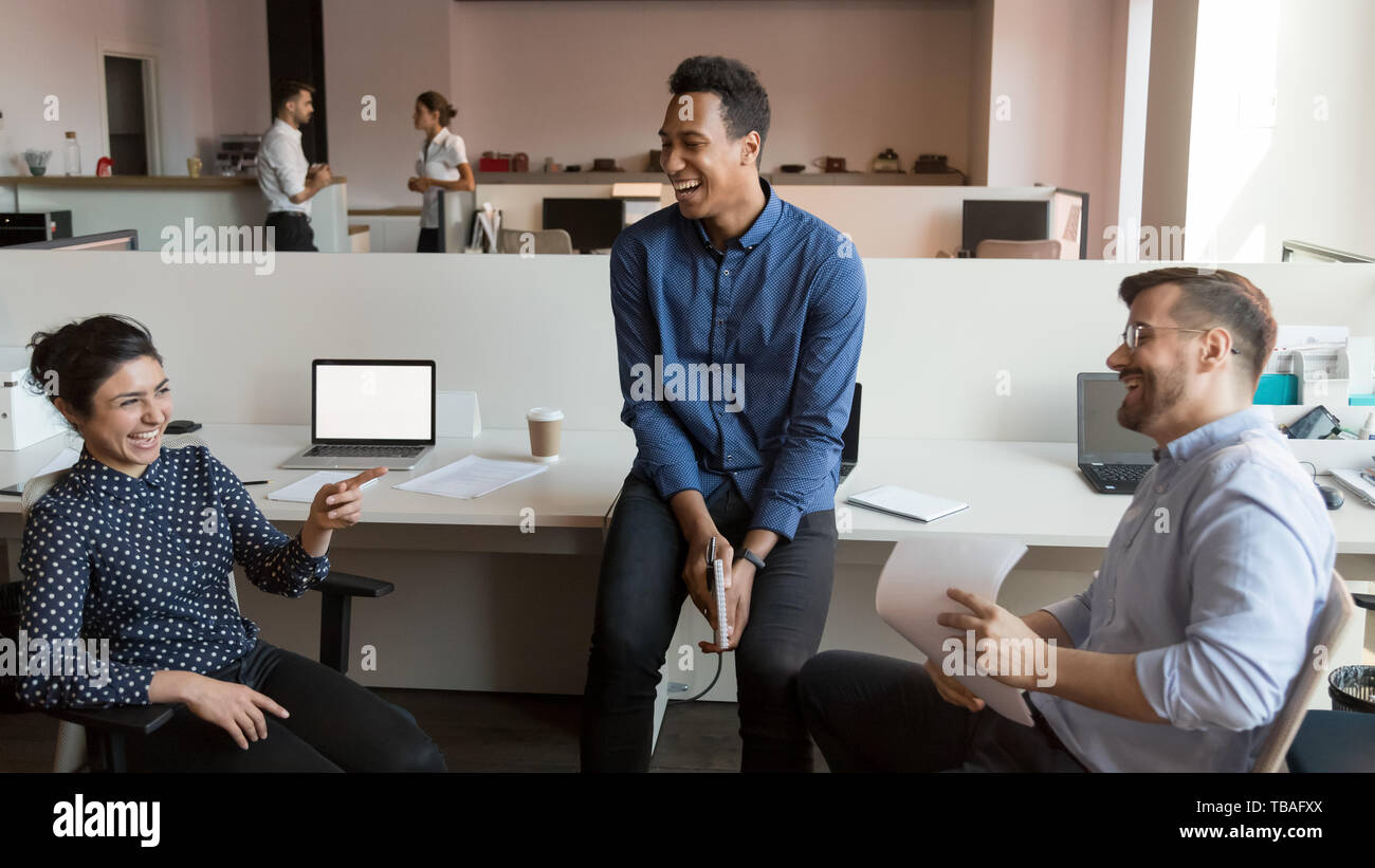 Smiling multiethnic colleagues laugh talking at informal team meeting ...