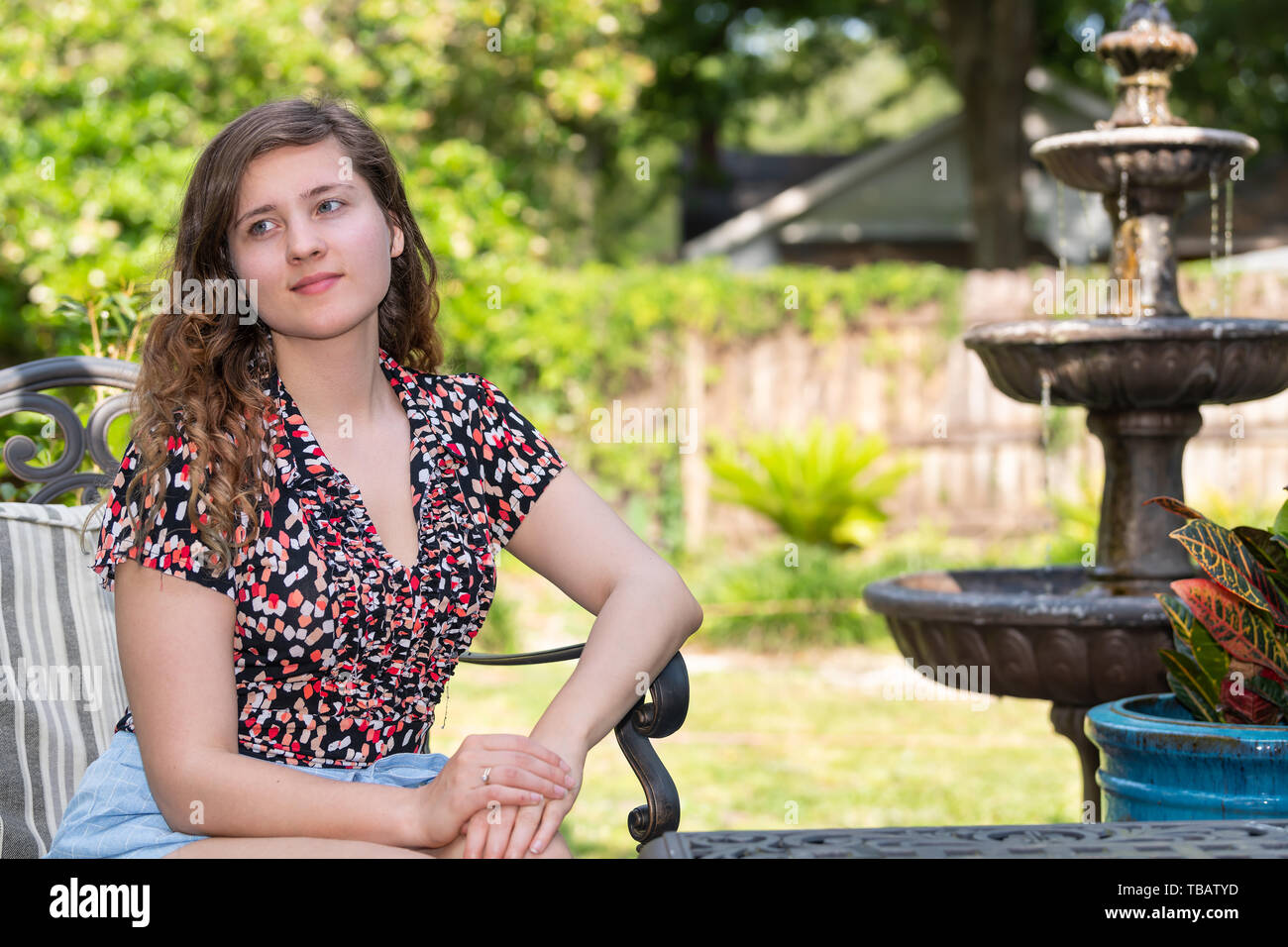 Young happy woman sitting on patio chair in outdoor spring garden in ...