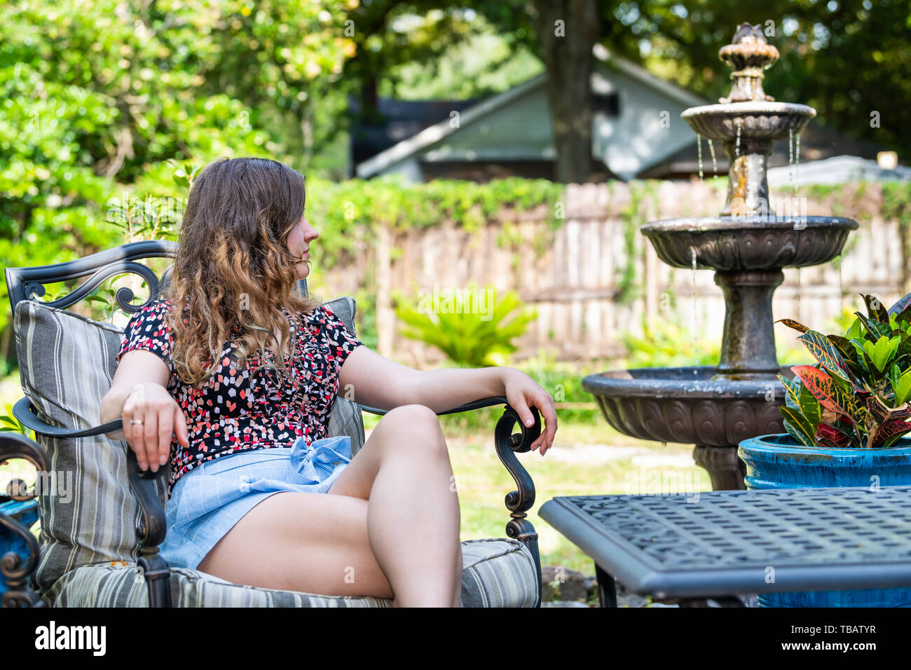 Young woman sitting on patio chair in outdoor spring garden in backyard ...
