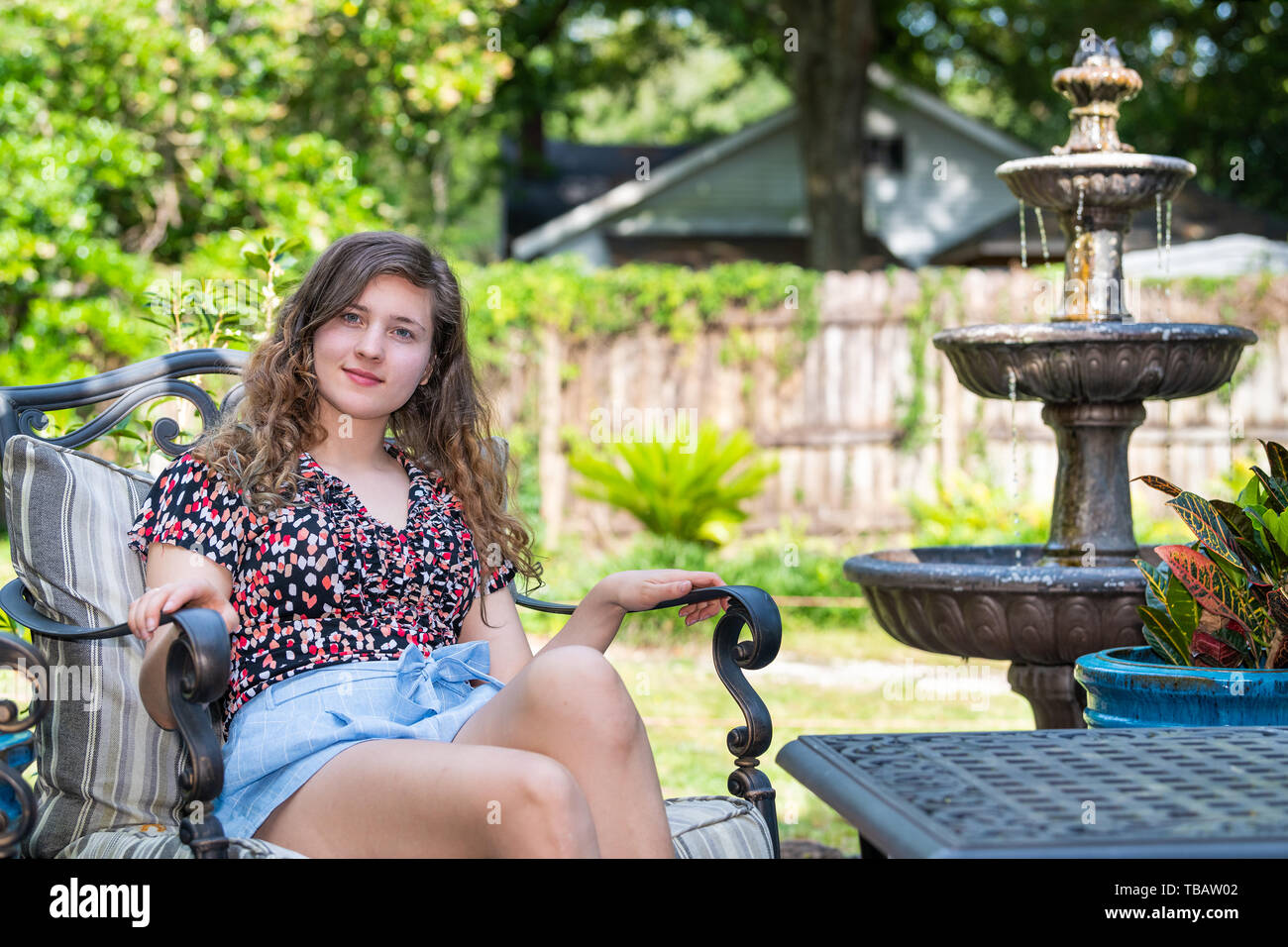 Young woman smiling sitting on patio chair in outdoor spring garden in ...