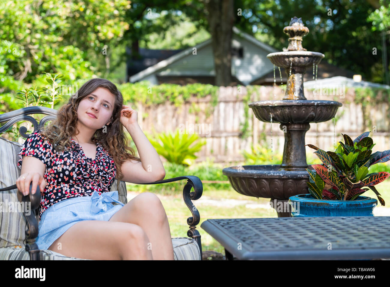 Young woman smiling looking up sitting on patio chair in outdoor spring ...