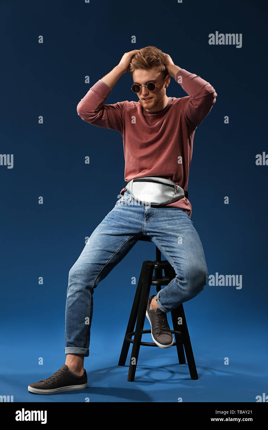 Fashionable young man sitting on stool against color background Stock ...