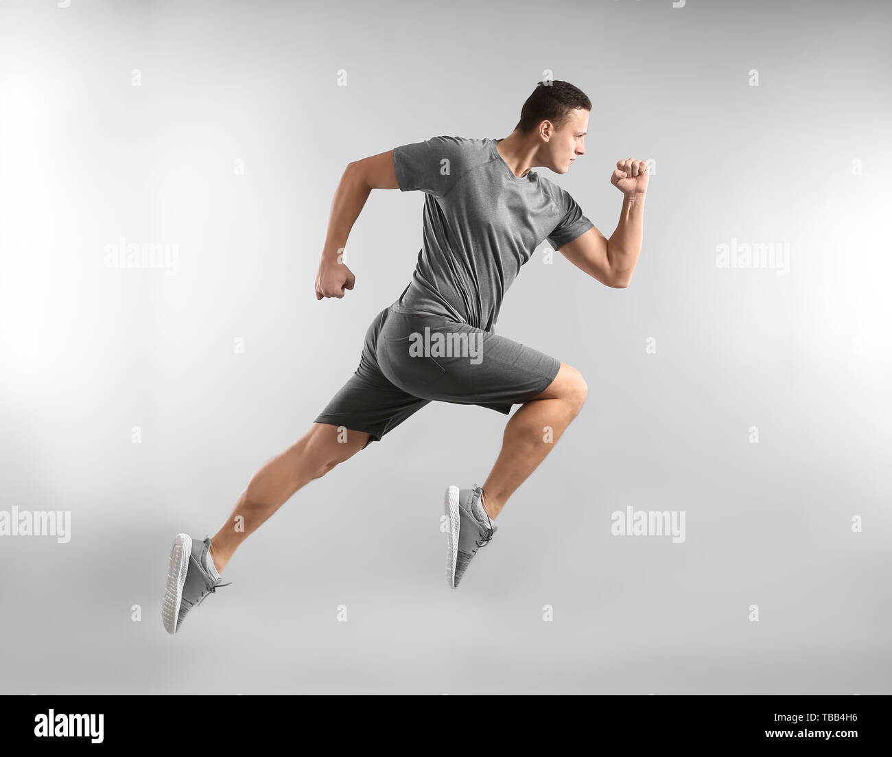 Sporty young man running against grey background Stock Photo - Alamy
