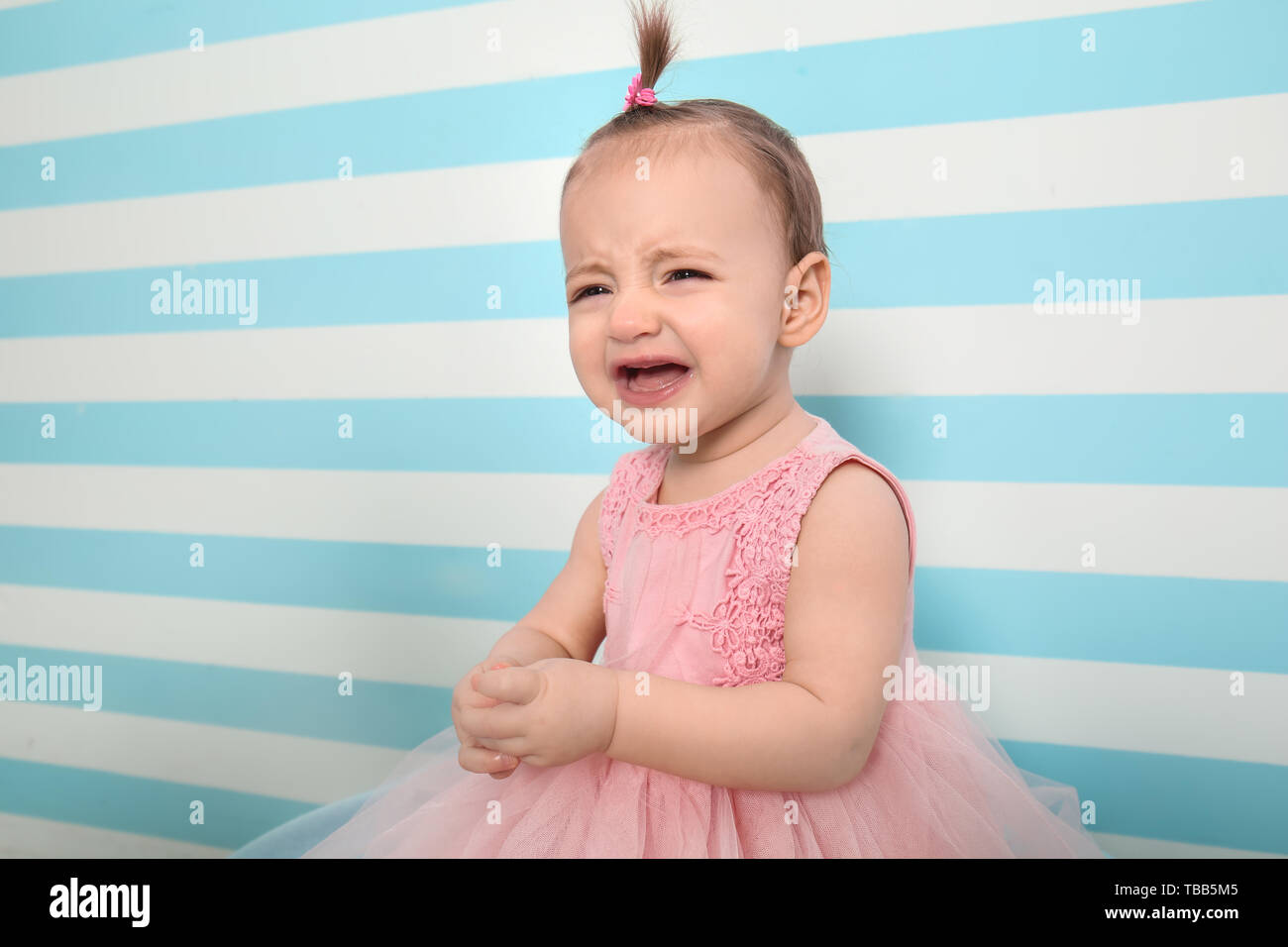 Cute crying baby girl on striped background Stock Photo - Alamy