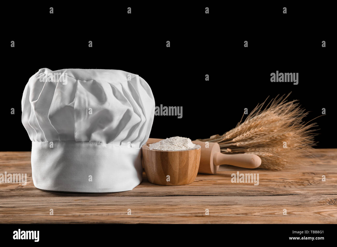Composition with chef's hat on wooden table against dark background ...