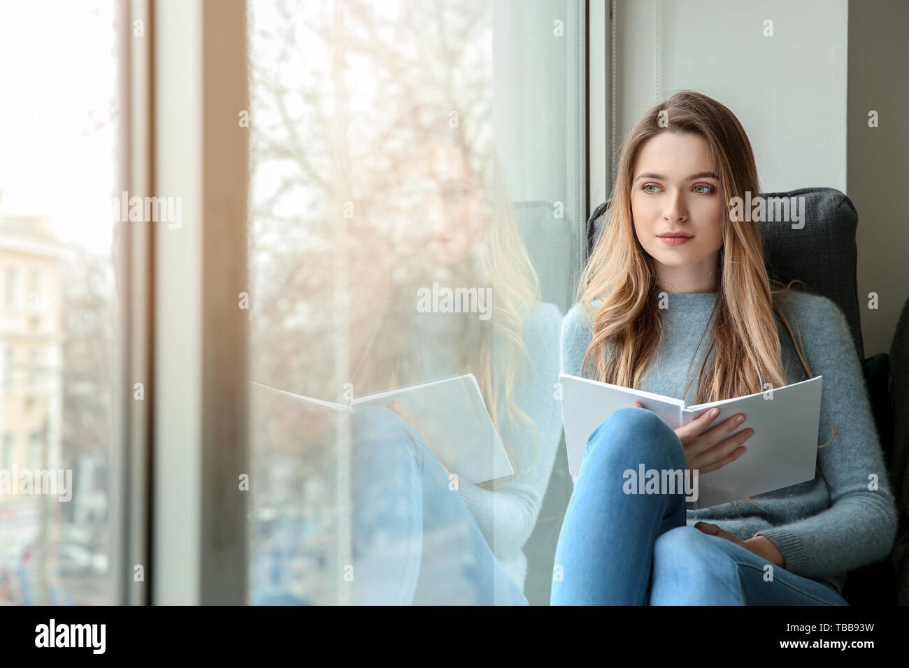 Beautiful young woman reading book while sitting on window sill Stock ...