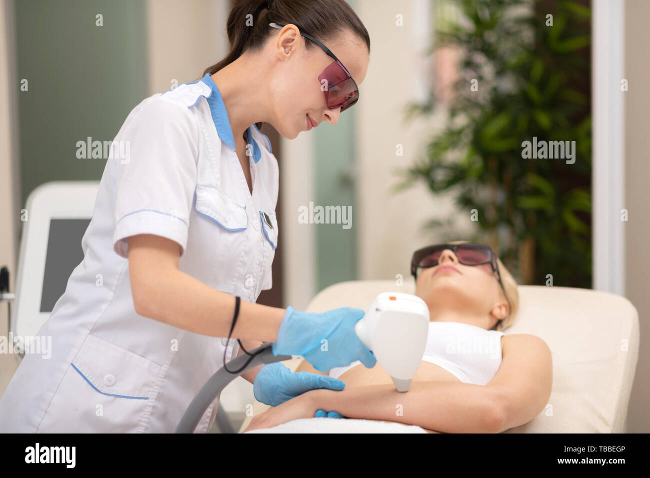 Laser depilation. Dark-haired professional master wearing uniform doing ...