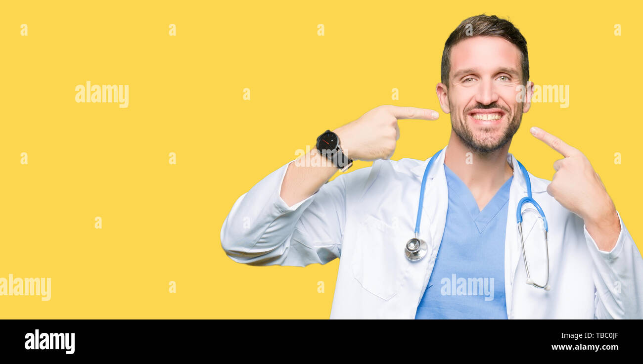 Handsome doctor man wearing medical uniform over isolated background ...