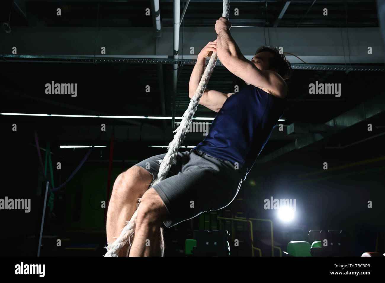 Young sporty man climbing up the rope in gym Stock Photo - Alamy