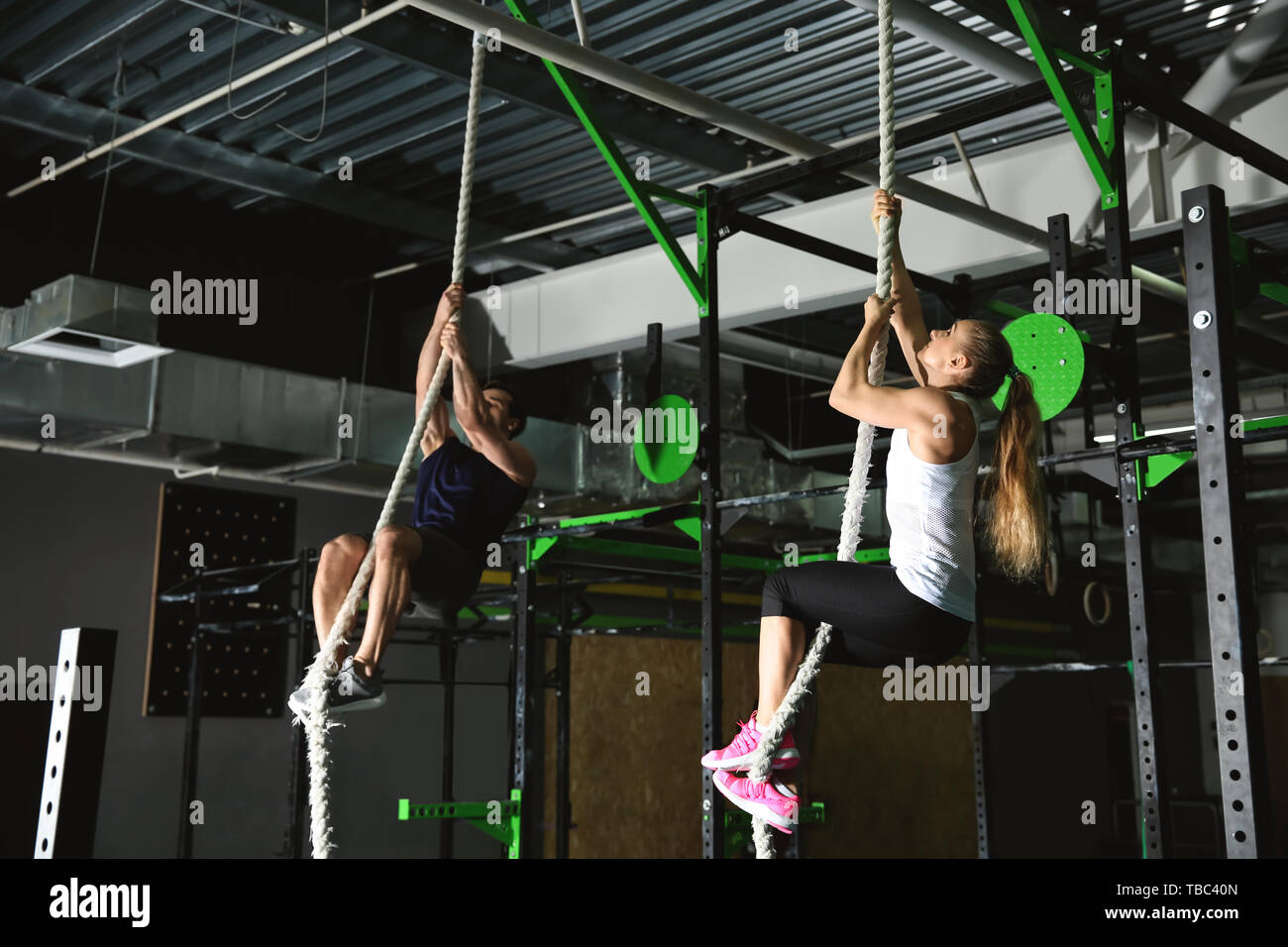 Young sporty couple climbing up the rope in gym Stock Photo - Alamy