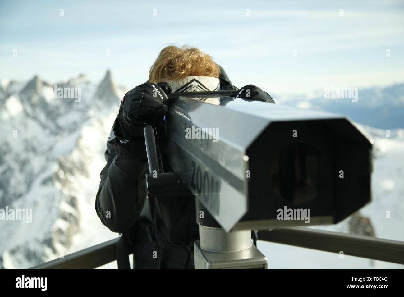 Human in snow outfit uses a zoom lens at high altitude, gazing past the ...