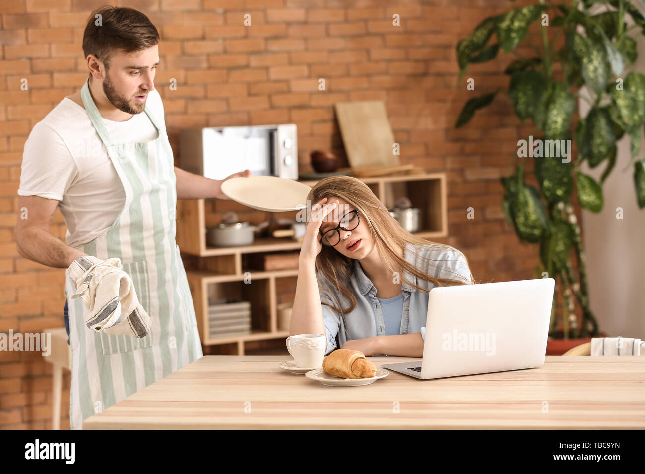 Tired wife working while her indignant husband doing chores at home ...