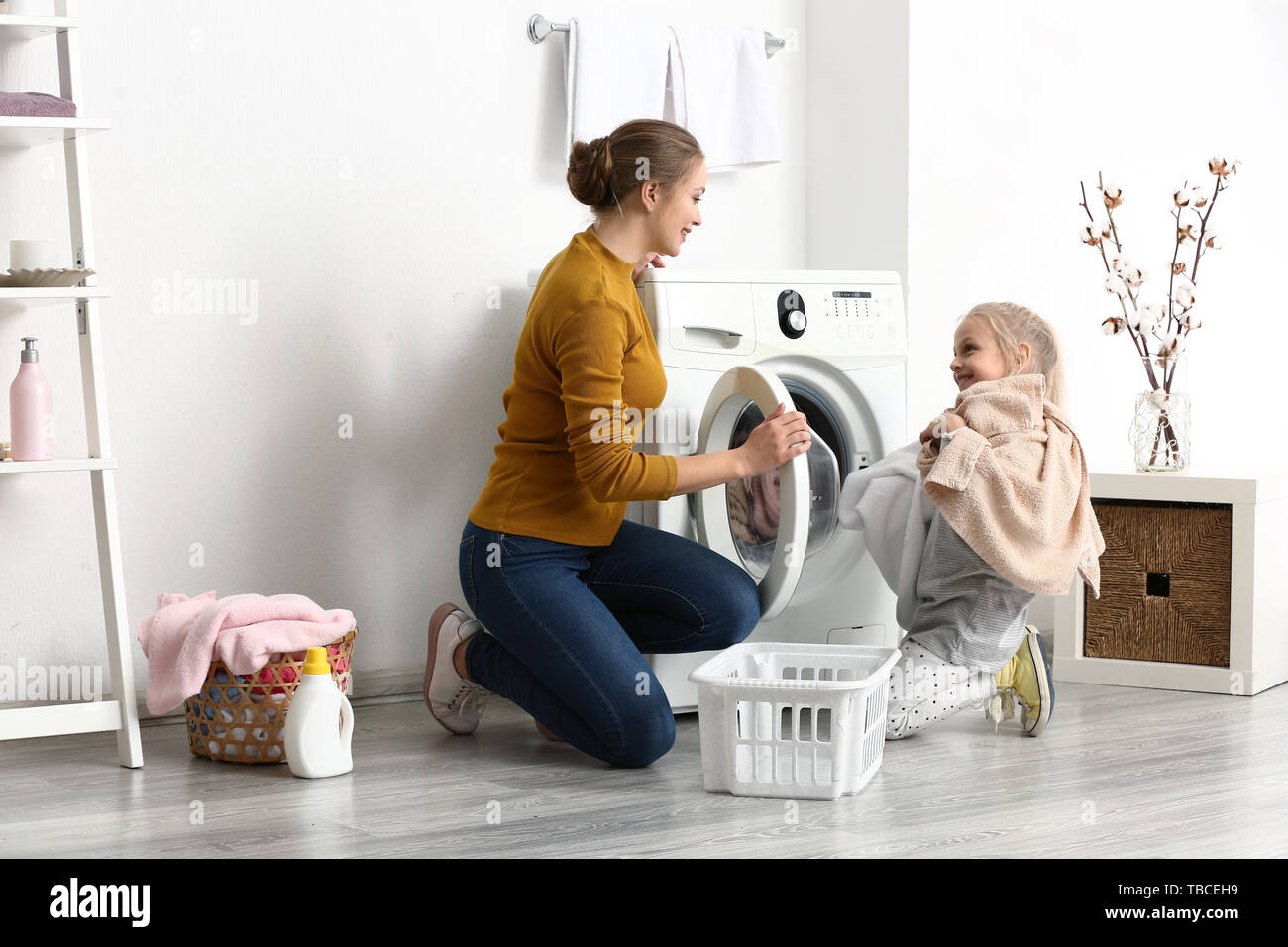 Young woman and her little daughter doing laundry at home Stock Photo ...