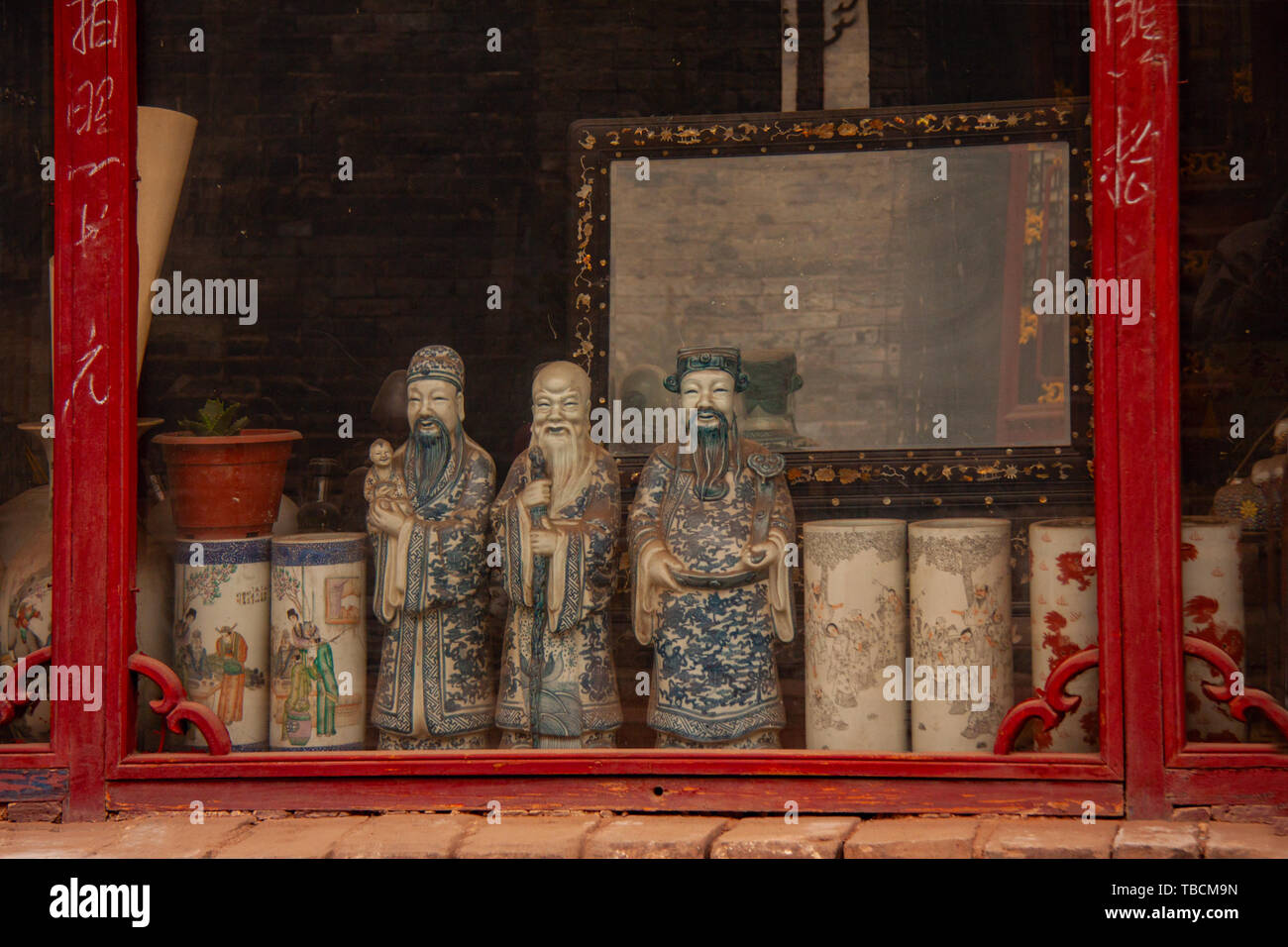 Antique old Chinese figures and vases on display in a red window frame ...