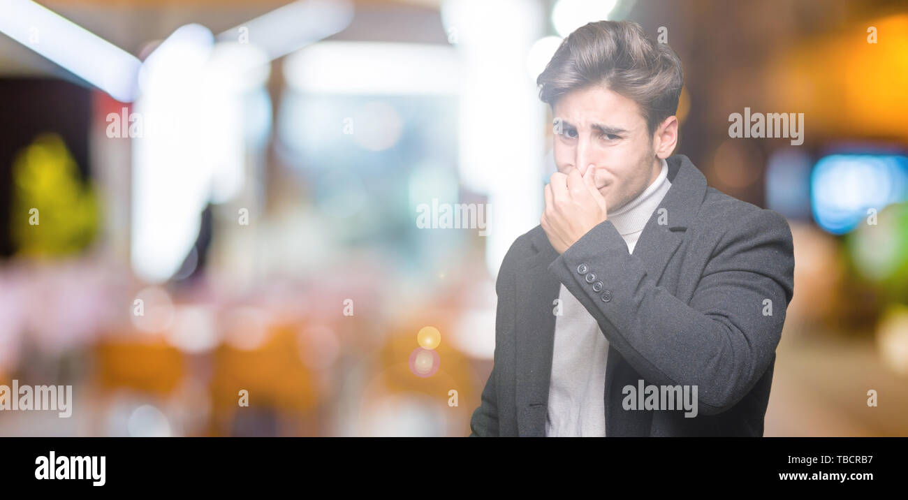 Young elegant man wearing winter coat over isolated background smelling ...