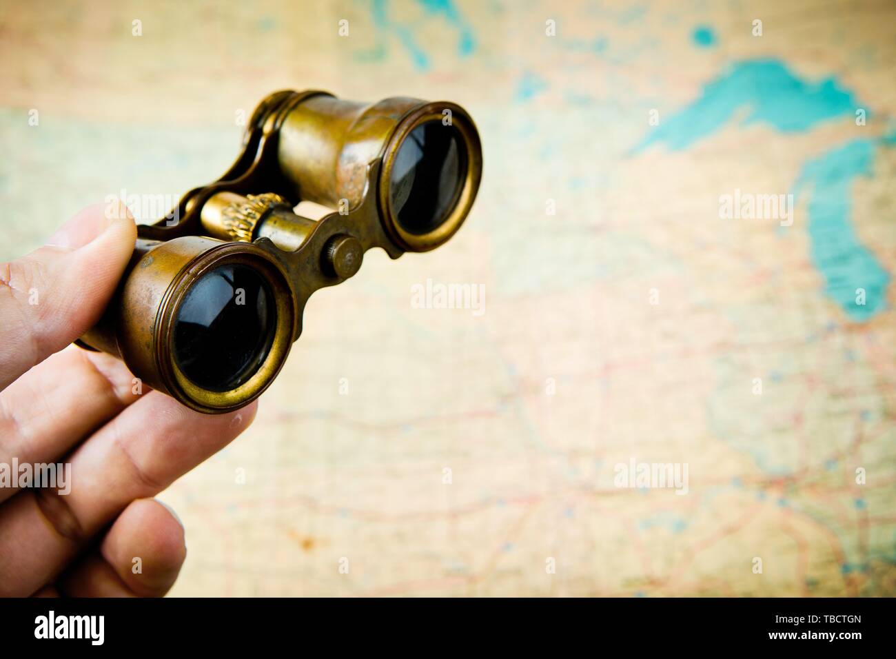 Fingers holding vintage brass binoculars, blurry map on the background ...