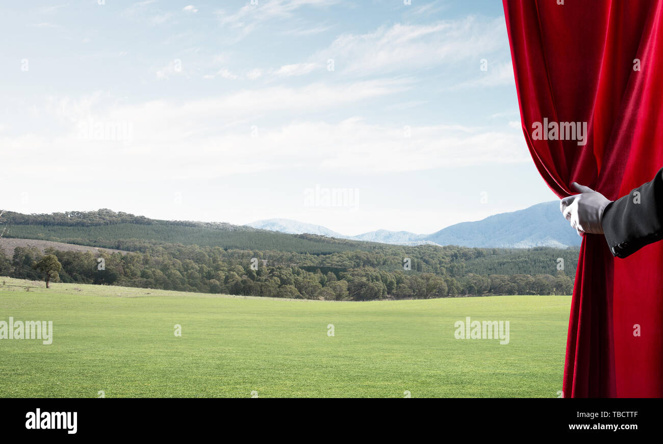 Green meadow behind red curtain and hand holding it Stock Photo - Alamy