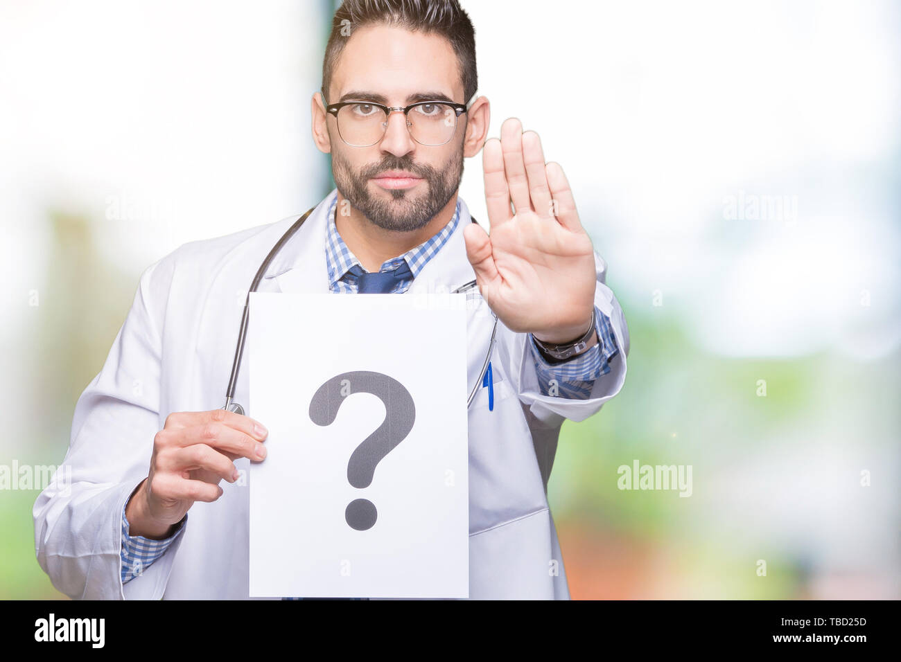 Handsome young doctor man holding paper with question mark over ...