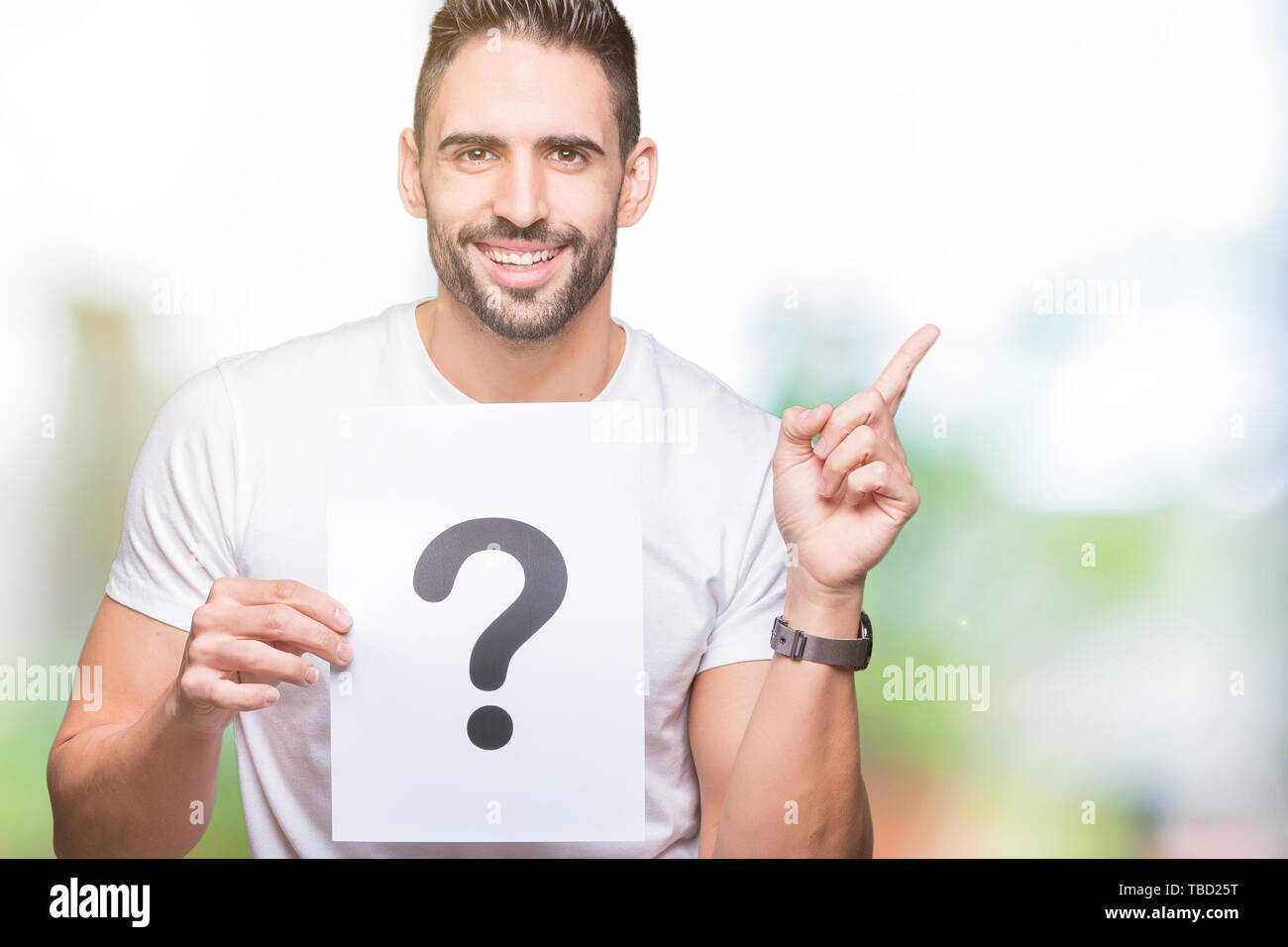 Handsome young man holding paper with question mark over isolated ...