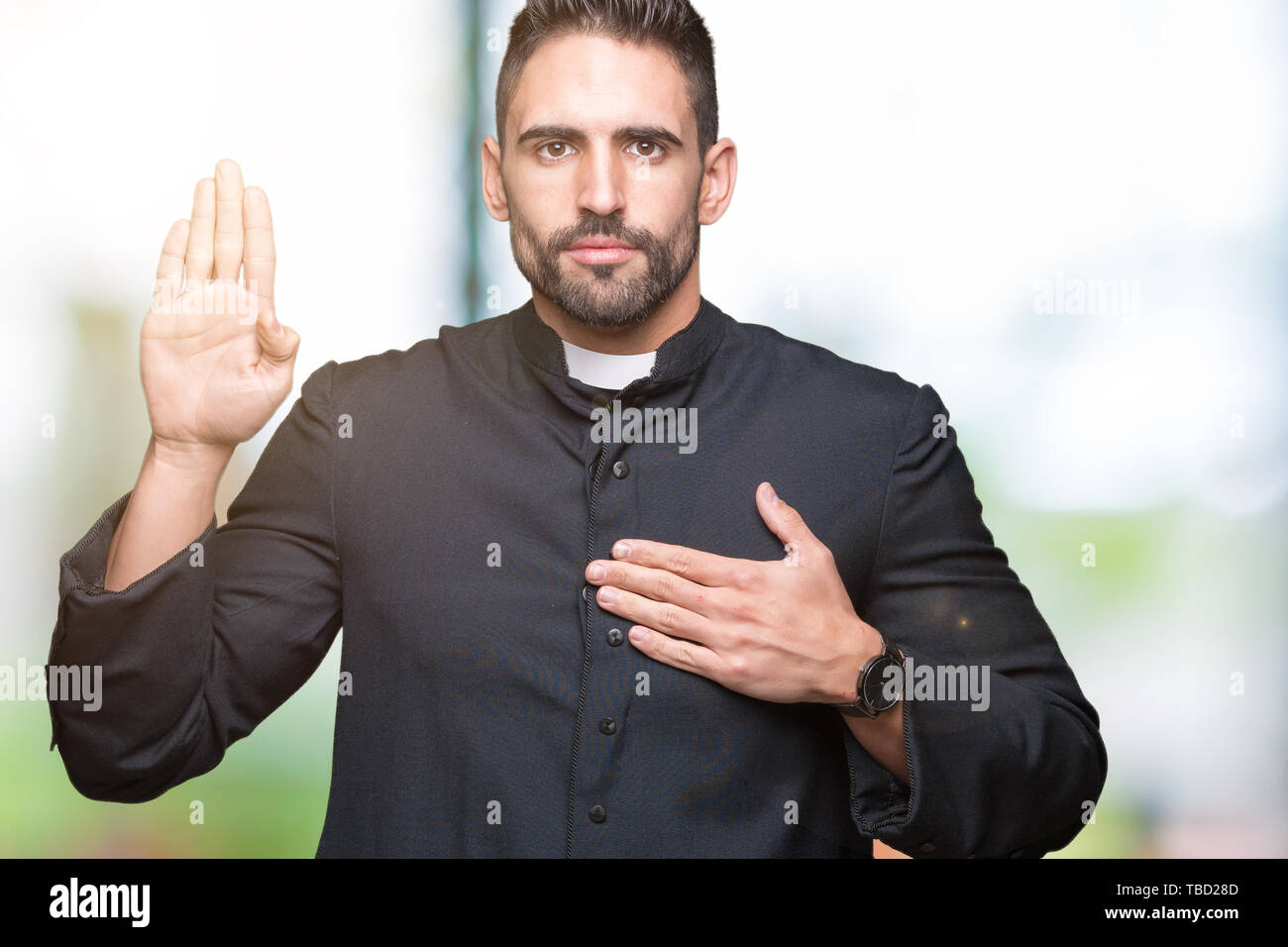 Young Christian priest over isolated background Swearing with hand on ...