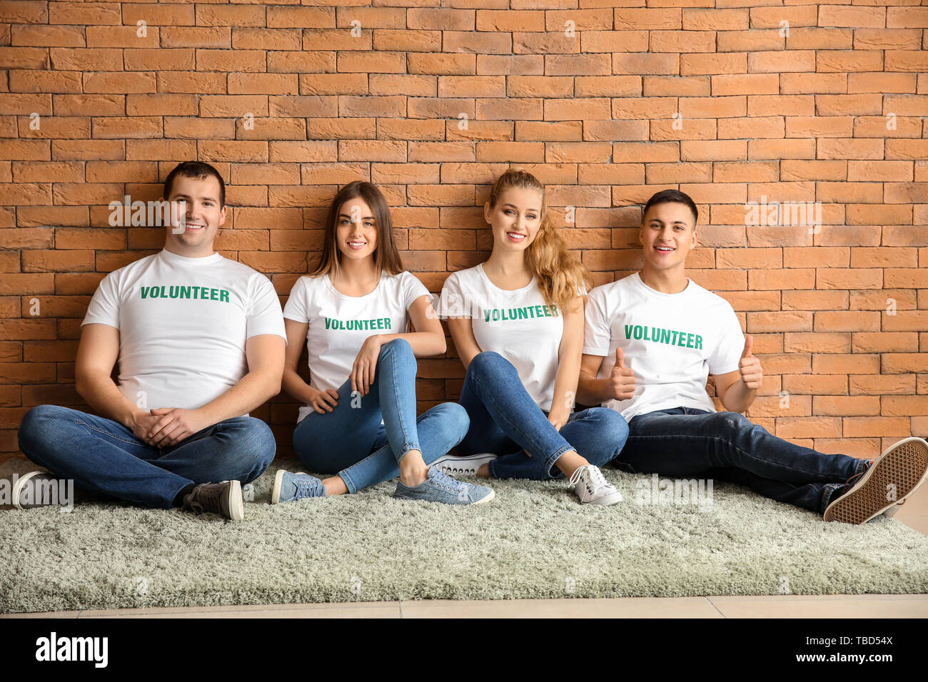 Team of young volunteers sitting near brick wall Stock Photo - Alamy