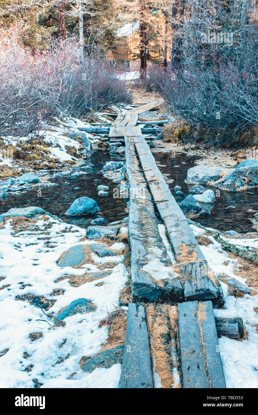 Footpath in forest over mountain stream. Bridge of boards under snow ...