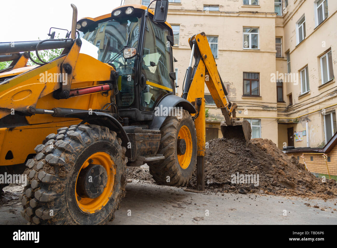 Excavator digs a trench. Repair work in the courtyard of a residential ...
