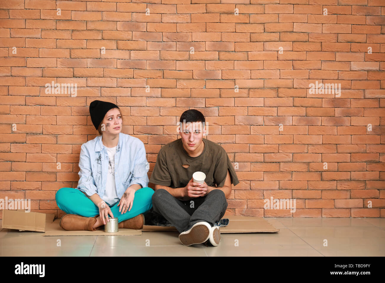 Poor homeless people sitting near brick wall Stock Photo - Alamy