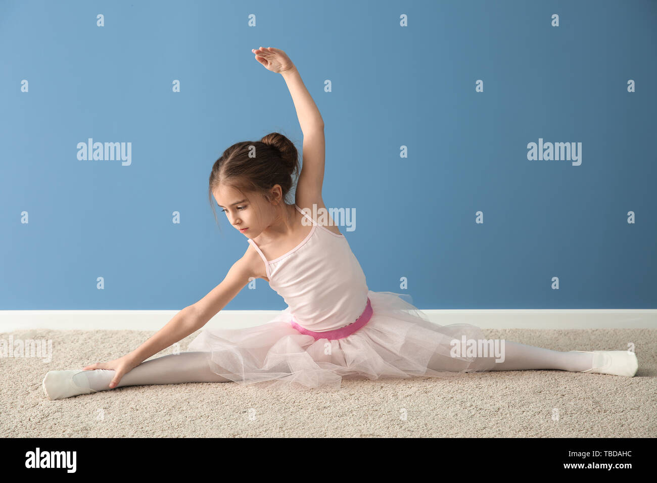 Cute little ballerina stretching near color wall Stock Photo - Alamy