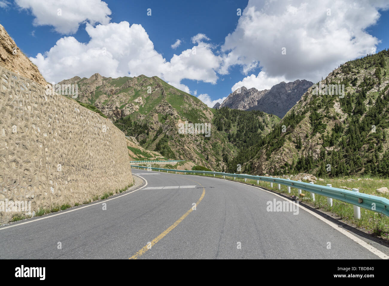 G217 Duku Highway bend in alpine forest under summer blue sky and white ...