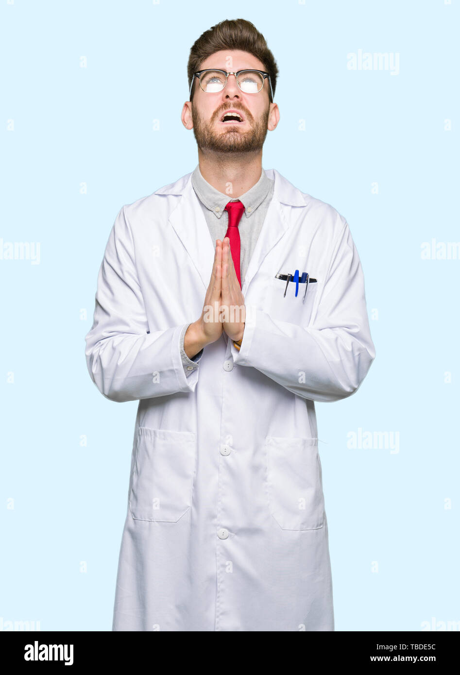 Young handsome scientist man wearing glasses begging and praying with ...