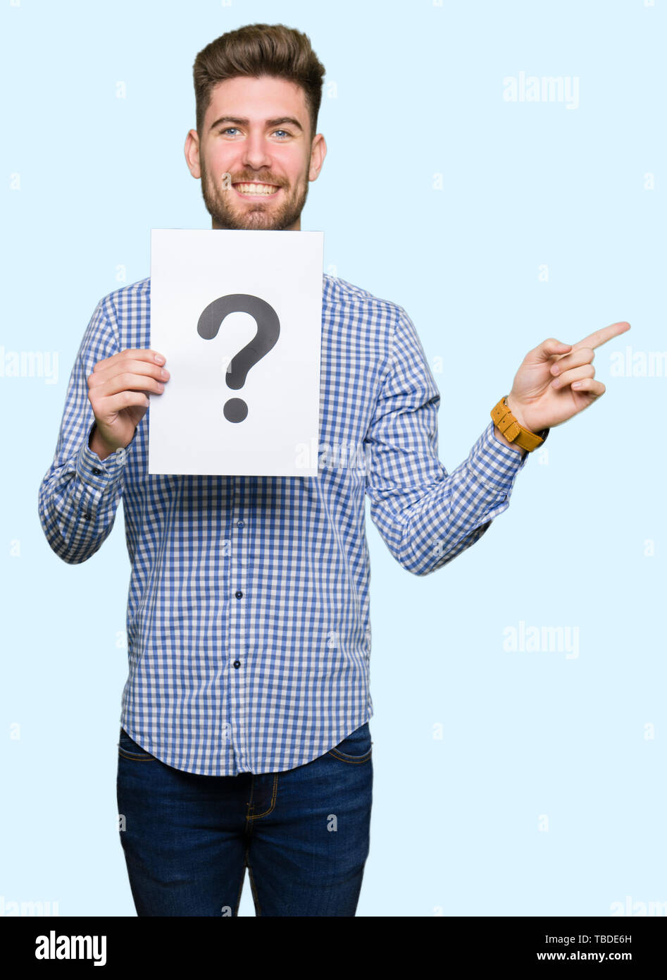Young handsome man holding paper with question mark very happy pointing ...