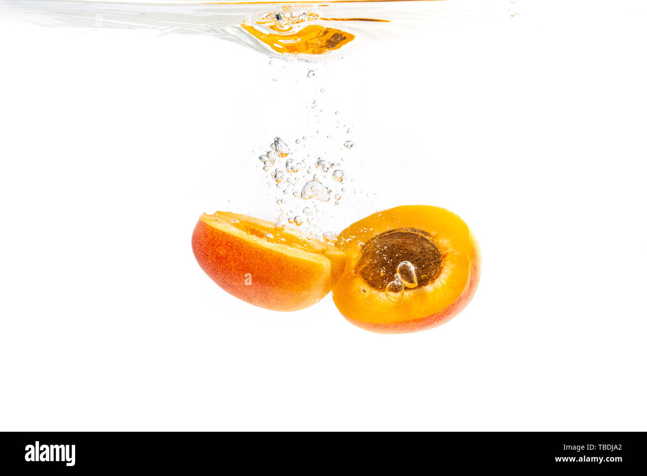 Fresh ripe apricot split in half falling in the clear water, isolated ...