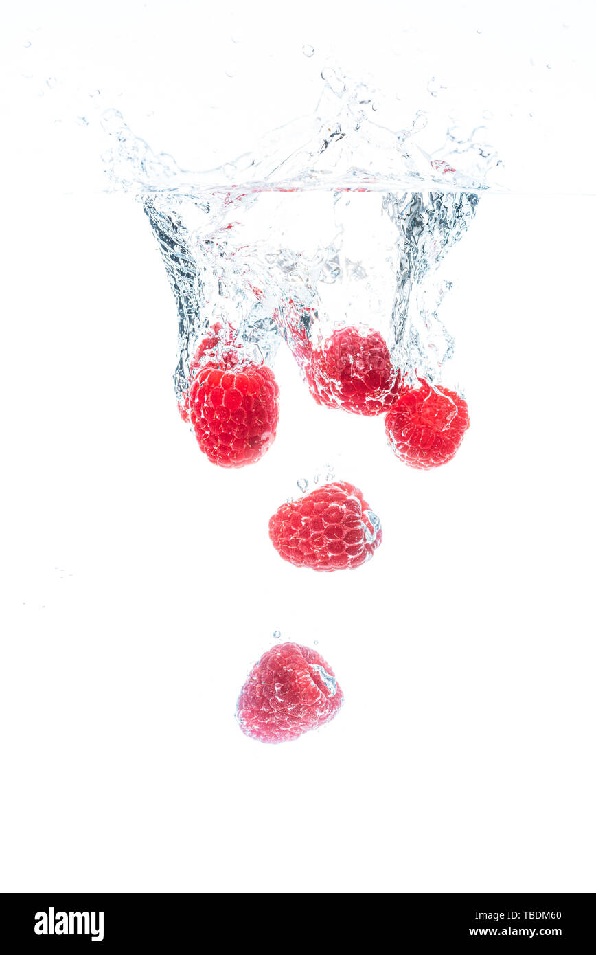 Raspberries falling into crystal clear water. Isolated on white ...