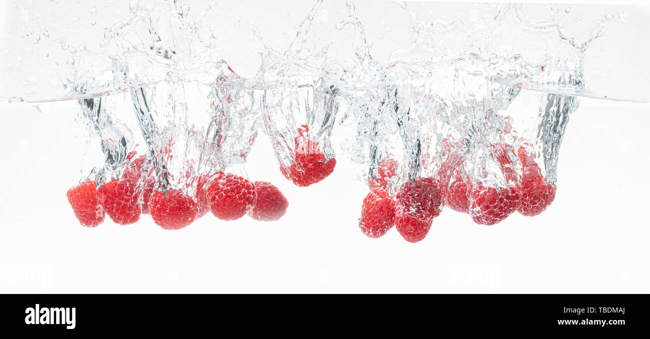 Panoramic photo of raspberries falling into crystal clear water ...