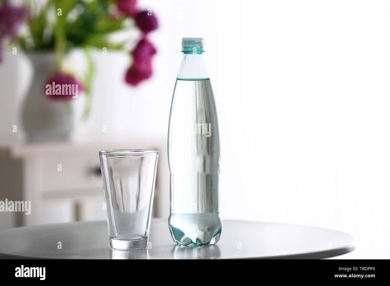 Bottle and glass of water on table in room Stock Photo - Alamy