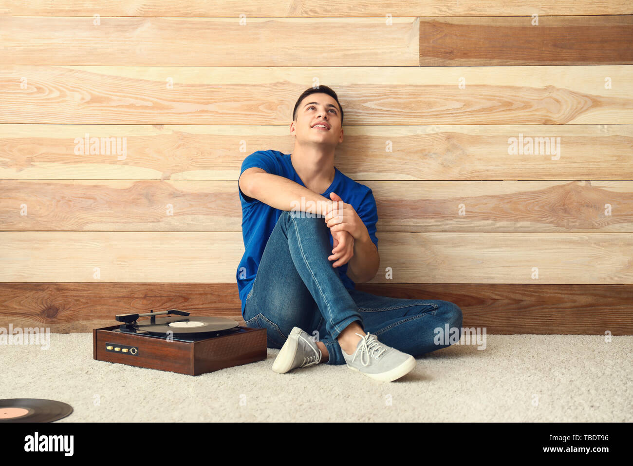 Young man listening to music on record player near wooden wall Stock ...