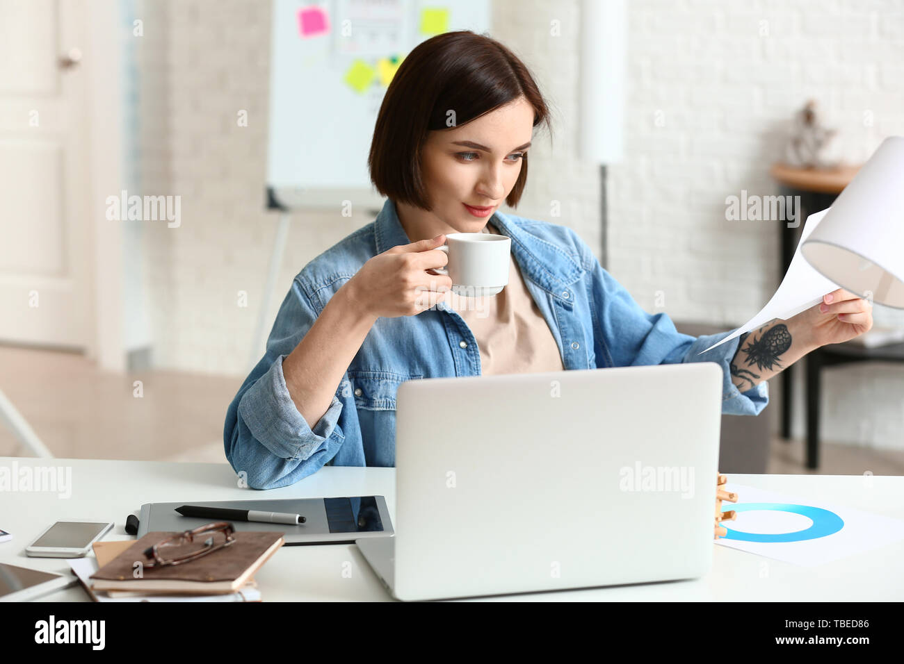 Female designer drinking coffee while working in office Stock Photo - Alamy