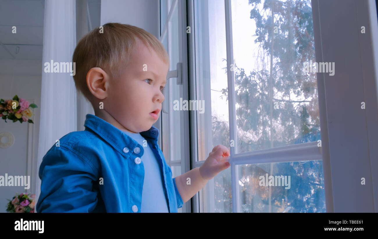 Pensive little boy looking through window Stock Photo - Alamy