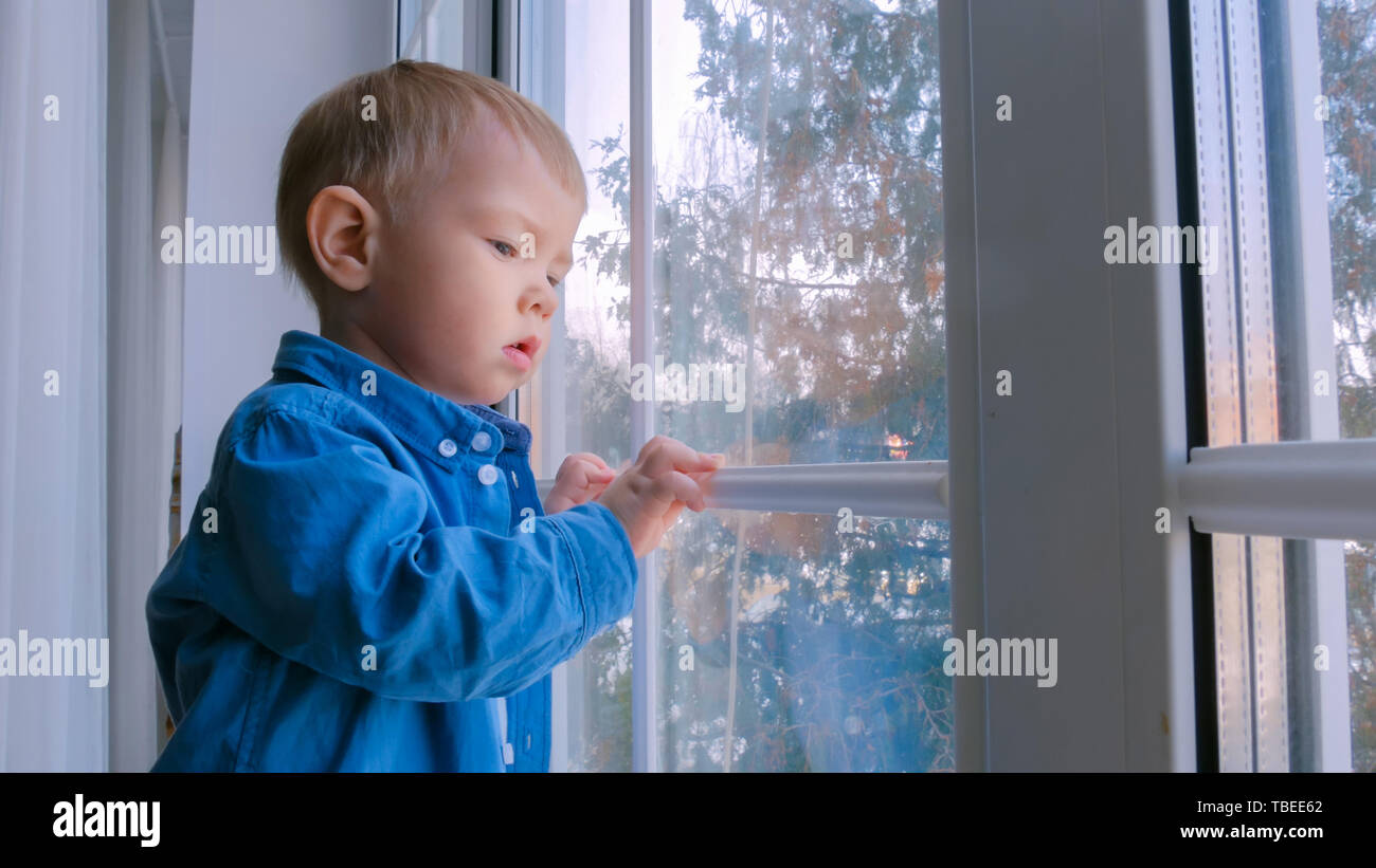 Pensive little boy looking through window Stock Photo - Alamy
