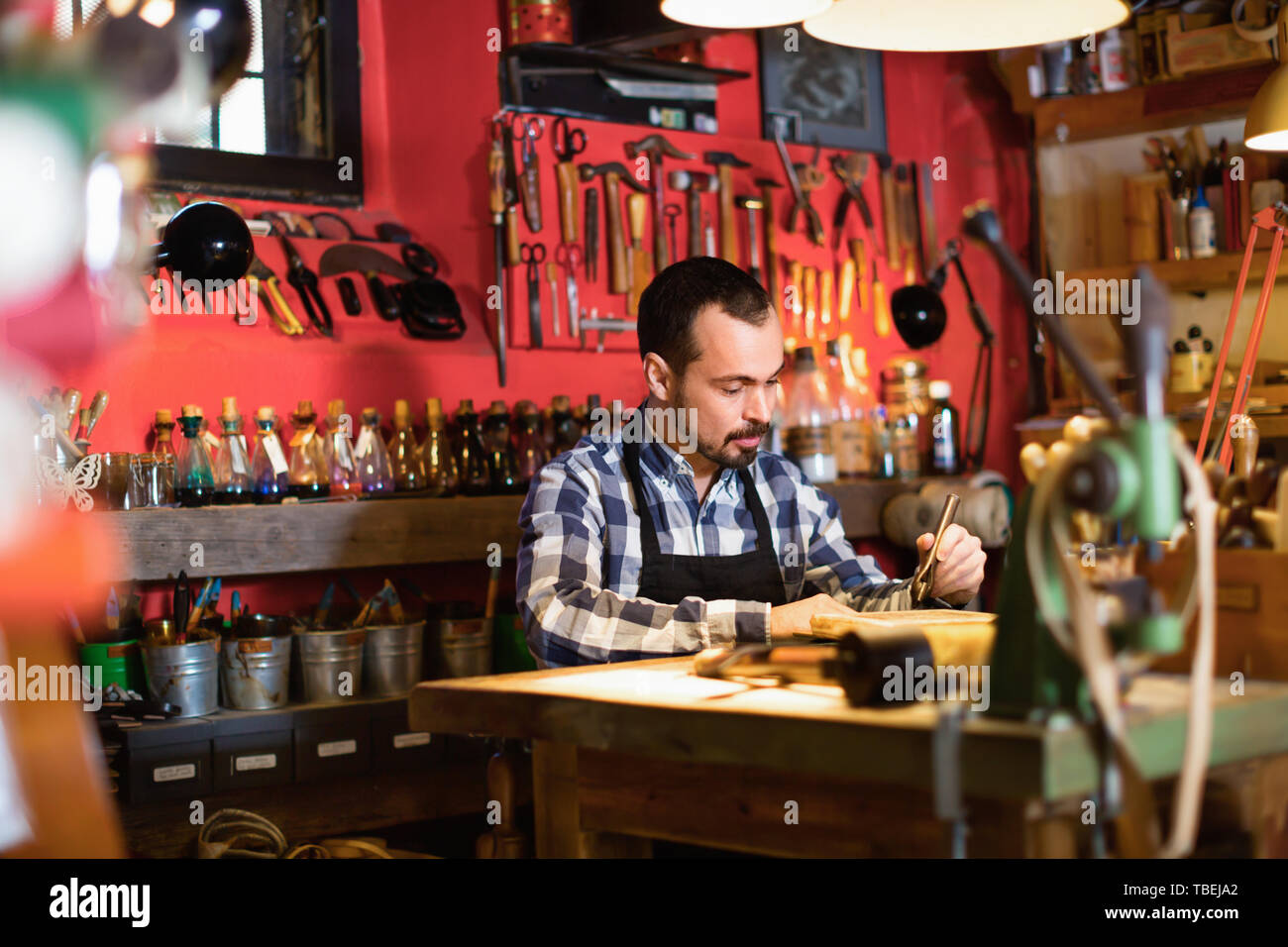 Diligent friendly smiling male worker working on leather for belt in ...