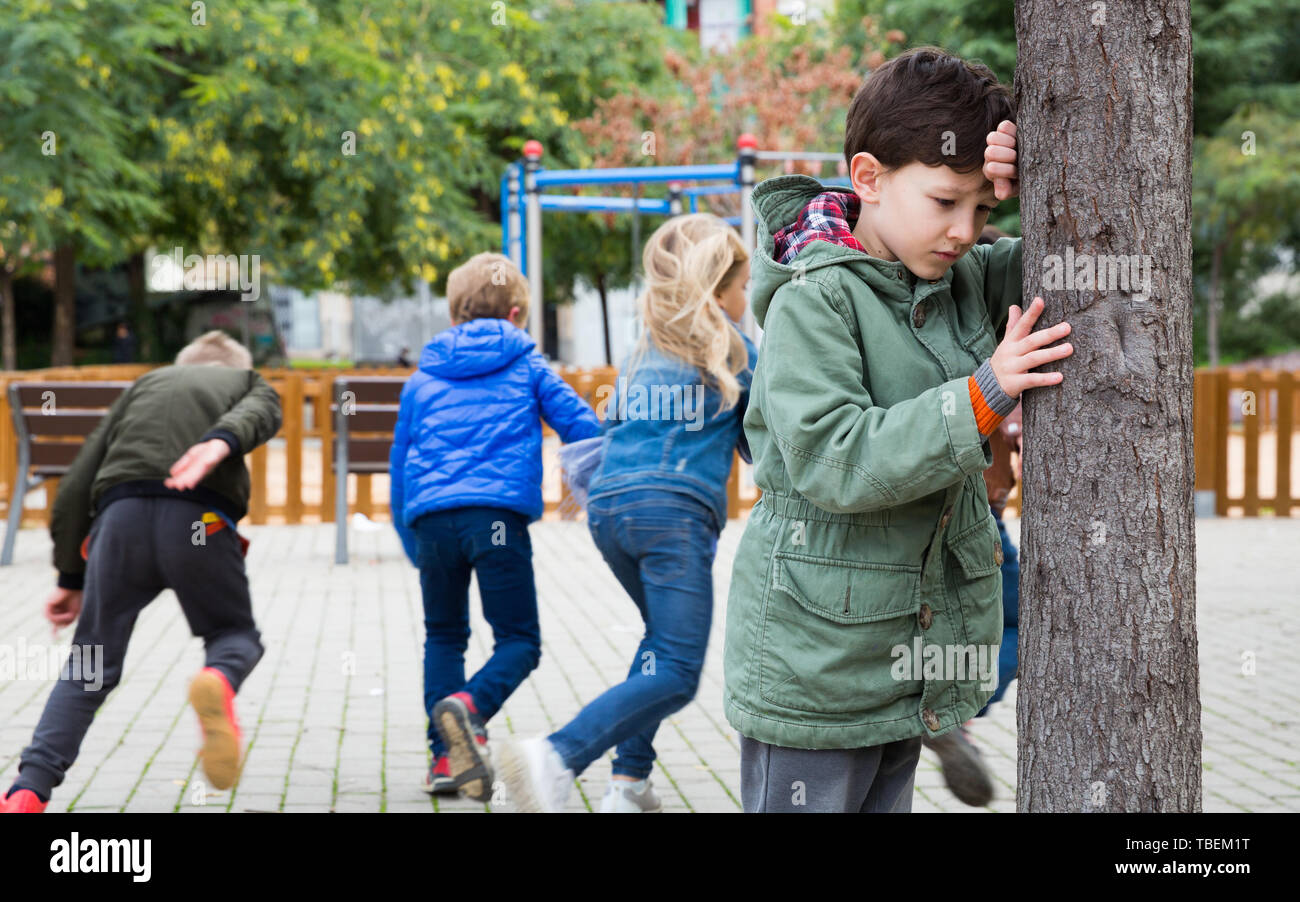 Children playing hide and seek outdoors. Boy standing near tree and ...