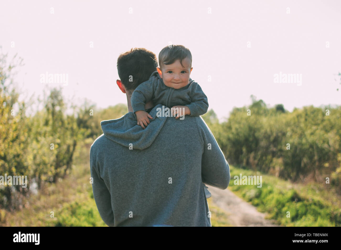 Cute baby boy on his dad's shoulders walking on road outdoors ...