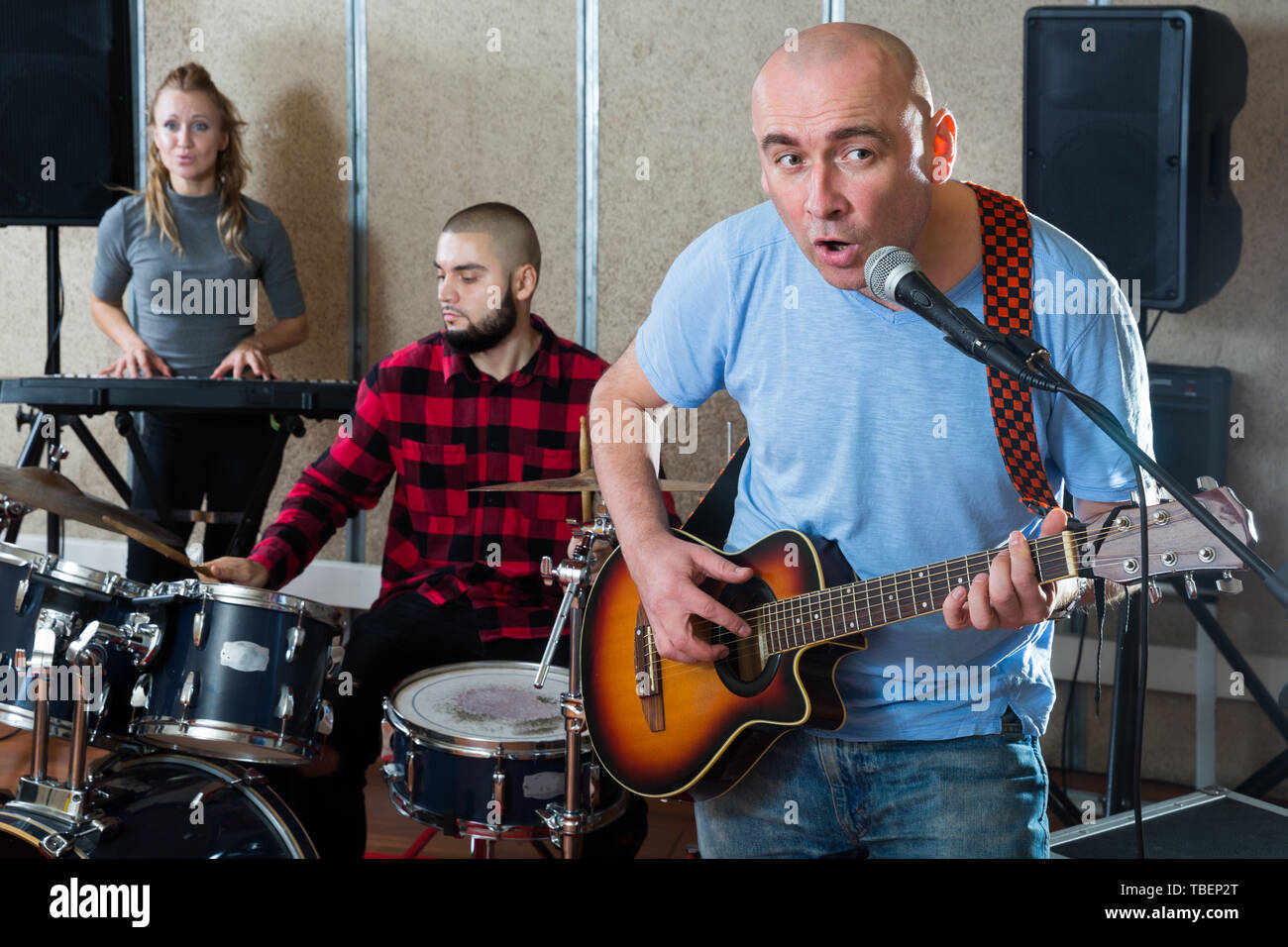 Nice male singer with guitar rehearsing with band of drummer and ...