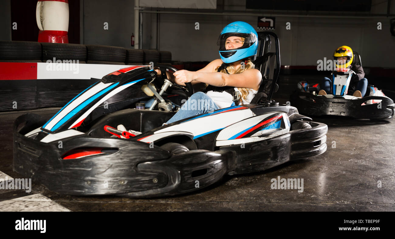 Young female in helmet and other people driving cars for racing in ...
