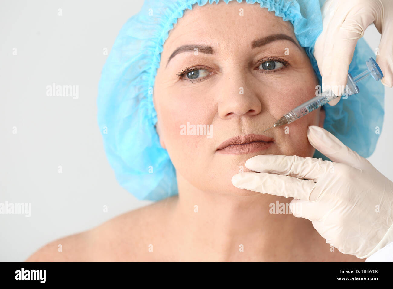 Mature woman receiving injection in face on light background Stock ...